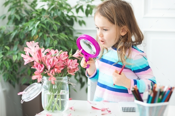 Emotional happy child girl looking at a flower through a magnifying ...