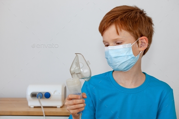 A child in a medical mask holds a nebulizer in his hands. Cough ...