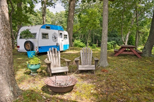 Small little camper in a campsite with picnic table, two Adirondack ...
