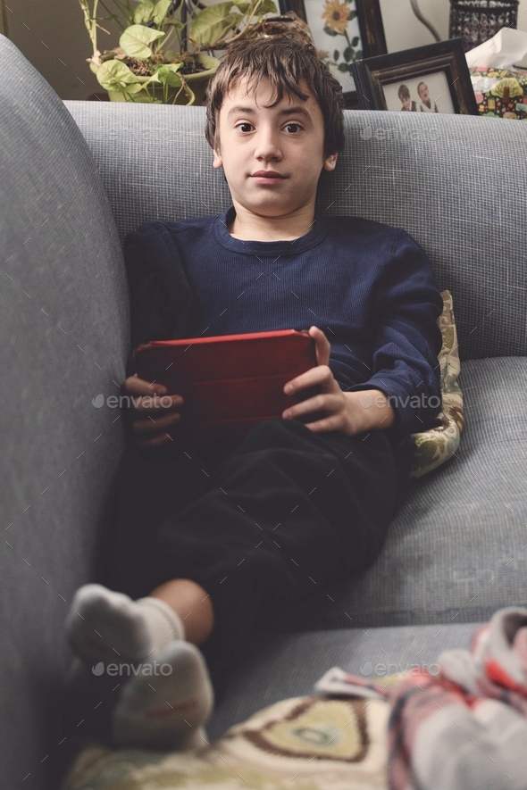 Gen z Boy sitting on the couch with his iPad making a surprised face ...