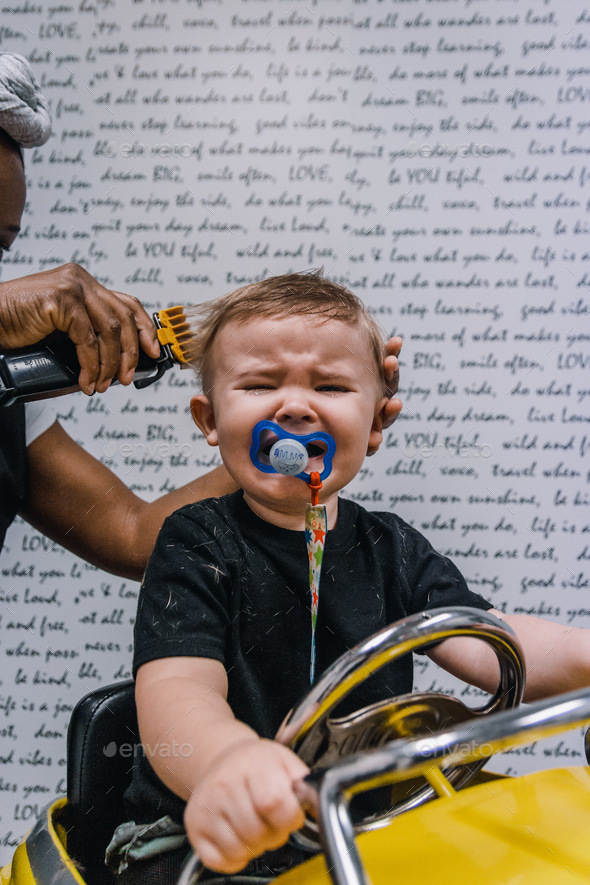 A little boy cries while getting a haircut in a kids yellow taxi cab ...