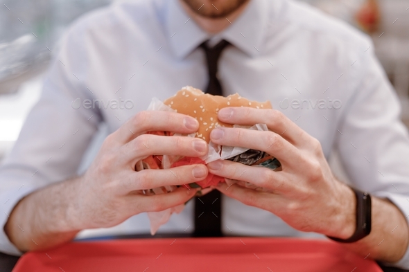 Office worker eating fast food burger and drink soda at food court in ...