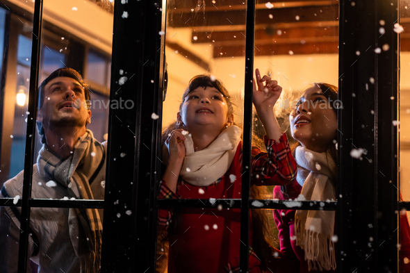 Adorable child look through the window and admiring first snow flakes ...