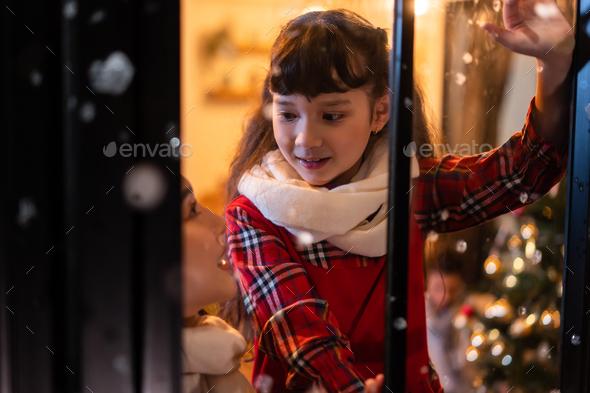 Adorable child look through the window and admiring first snow flakes ...