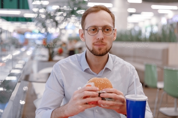Office worker eating fast food burger and drink soda at food court in ...