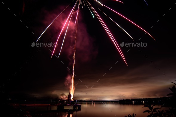 Fireworks on a country dock over lake with sky and clouds landscape ...
