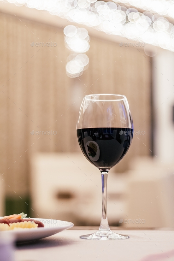Vertical photo of dark dry wine vine glass on blurred background. Light ...