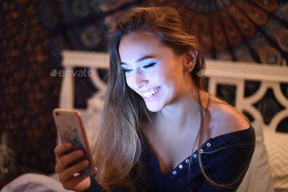 Technology young woman laughing at cell phone screen lighting her face indoors candid Stock ...