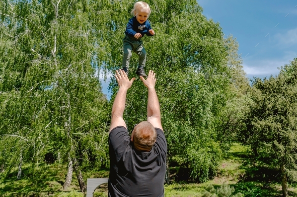 Father throwing little smiling baby child boy into air against green ...