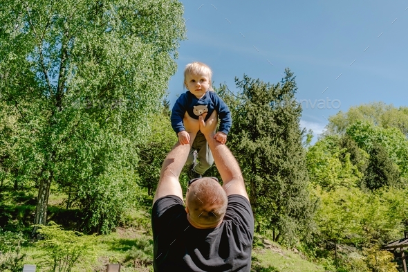 Father throwing little smiling baby child boy into air against green ...