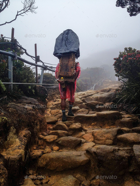 Man carries backpack and heavy items up a mountain. Porter climbing ...