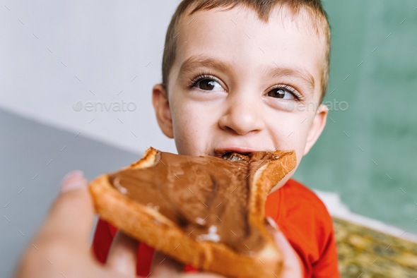 A child eats a toast with peanut butter from her mom’s hands. Stock ...
