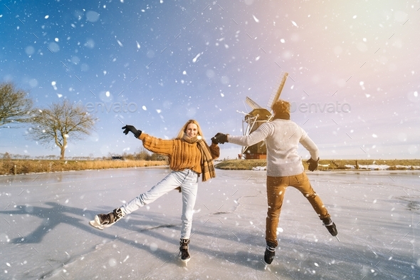 Loving couple having fun on ice in typical dutch landscape with ...