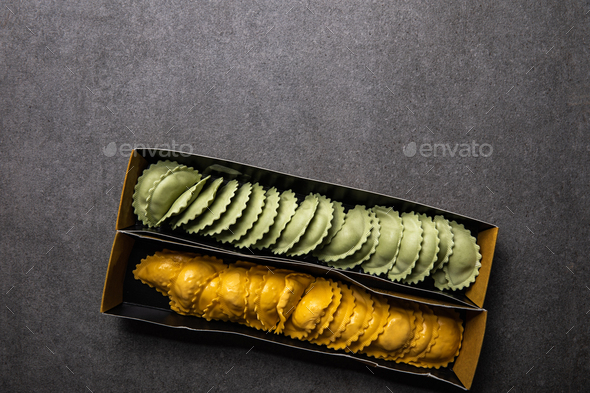 top view of green and yellow raw ravioli in cardboard box on grey ...