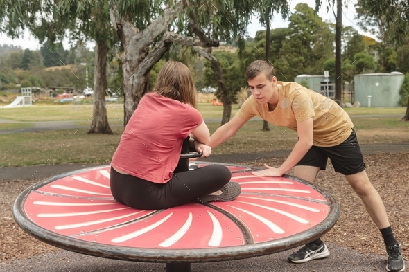 Young adolescent teenage boy pushing girl on playground equipment Stock ...