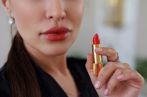 Young beautiful woman applying red lipstick in her big apartment ...