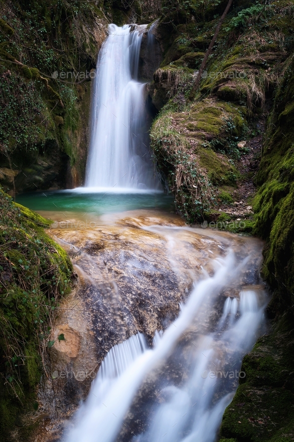 Waterfall of emerald green water in the woods Stock Photo by Graphico_