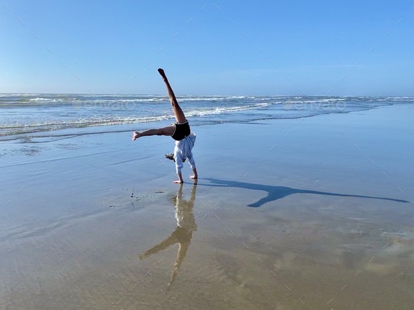 Preteen girl doing handstand or cartwheel on wet sand creating ...