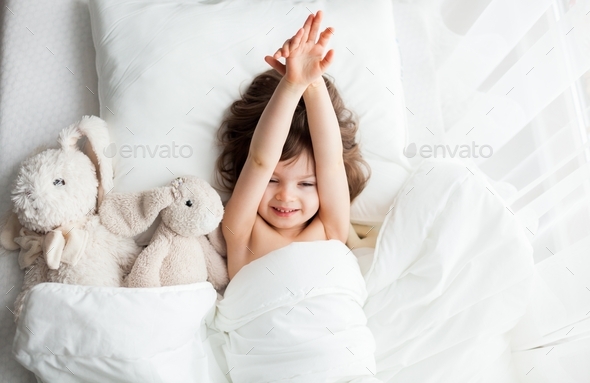 Adorable little girl stretching while lying in a white bed with her ...