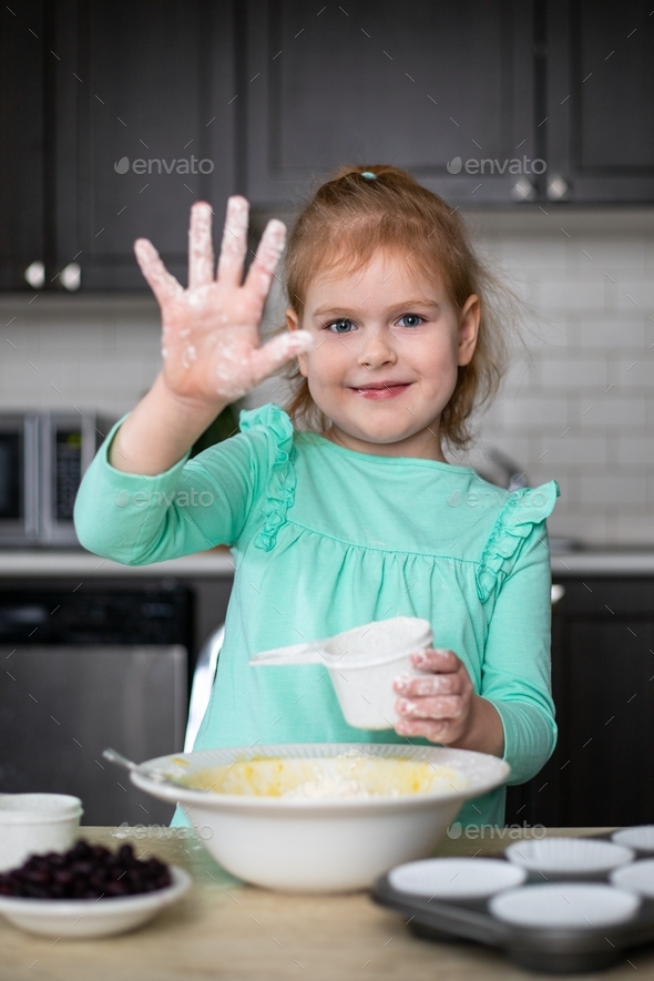 Little smilig girl having fun cooking in kitchen. Small child mixing ...