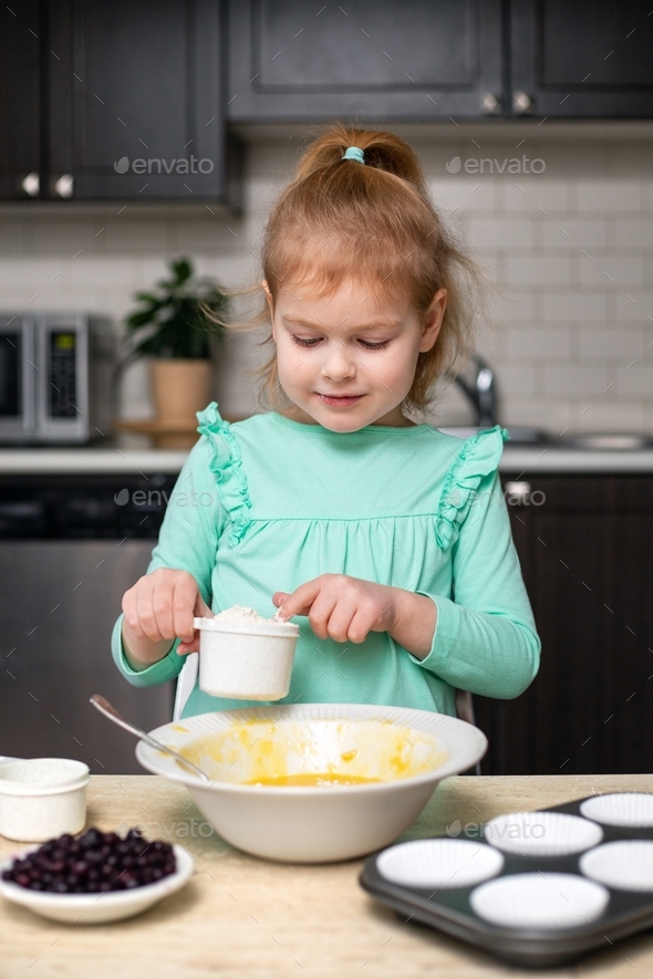 Little smiling cute girl mixing ingredients for baking homemade muffins ...