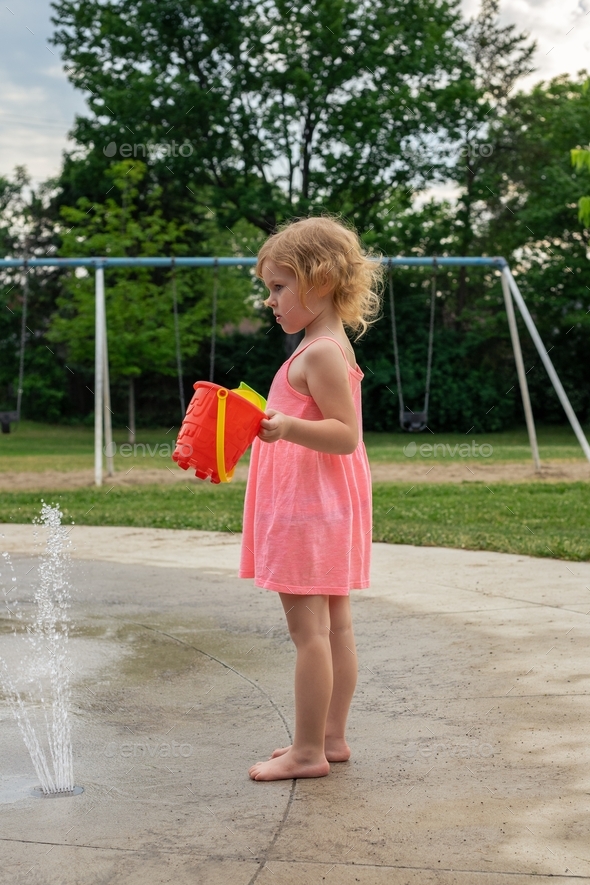 Little girl playing with bucket at water splash pad fountain in the ...