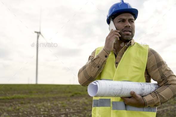 Latin male engineer standing on wind turbine field and talking on the ...