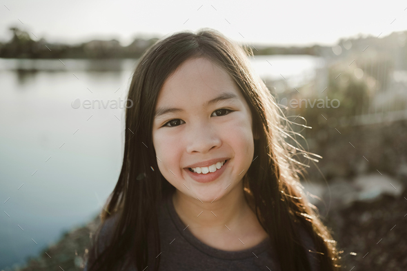 Happy mixed Asian preteen girl smiling by the waterfront, child ...