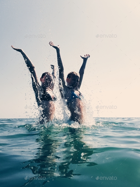 Two girls having fun in the ocean. Jumping and splashing water. Stock ...