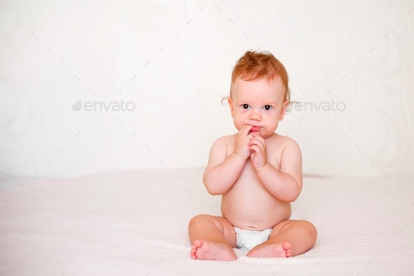 Cute little redhead baby boy in diaper sitting on the bed in light ...