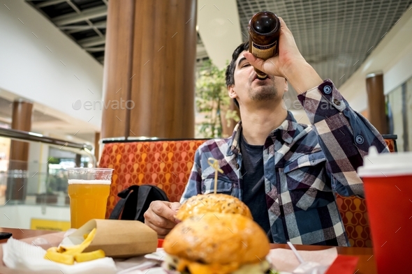 man eating burger fast food and drinking beer alone in the open area ...