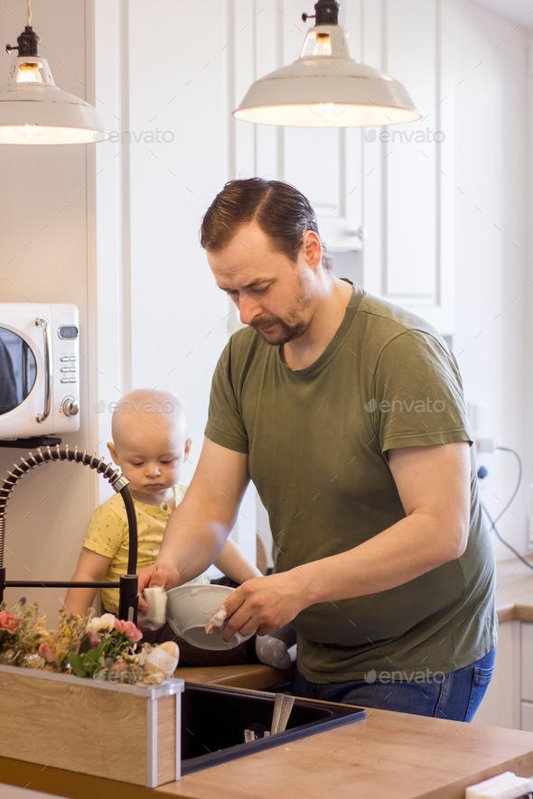 Father wash dishes on kitchen and little baby boy watching on it with ...