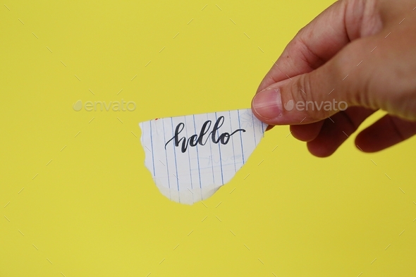 People hand holding piece of "HELLO" paper word closeup on yellow ...