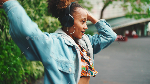 Smiling African girl walking down the street listening to music on ...