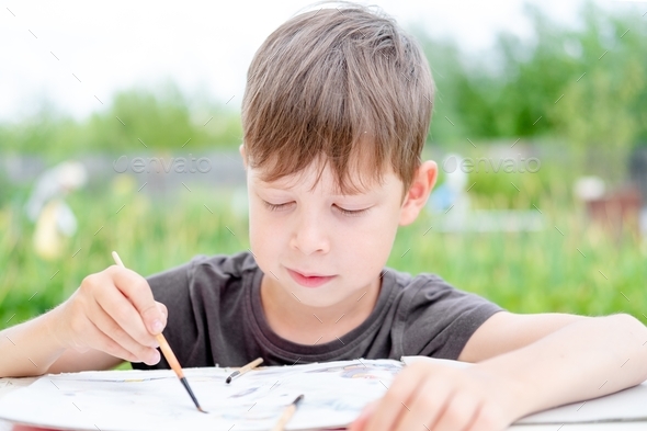 boy draws in nature. Drawing on the street. The boy draws with brushes ...