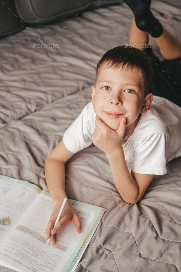 portrait of boy doing homework lying on gray sofa. A teenager writes in ...