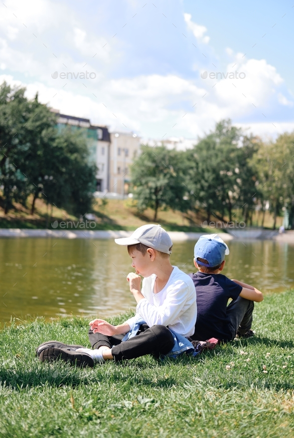 two boys are sitting with their backs to each other in a park near a ...