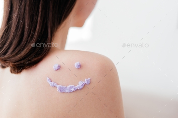 Smiley face made of purple cream scrub on shoulder of unrecognizable ...