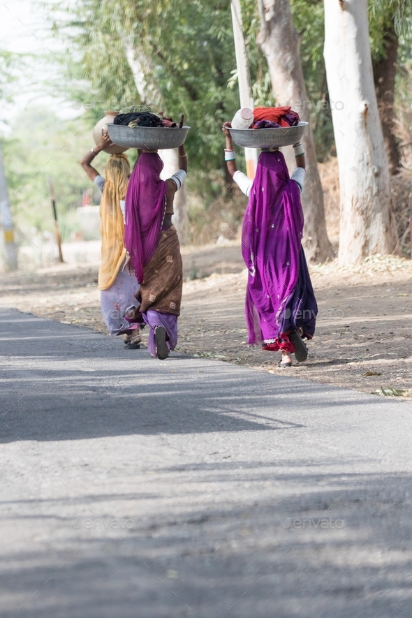 Indian women in traditional dress carry objects over their heads while ...