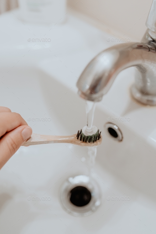 Bamboo natural toothbrush with toothpaste held in hand over a sink ...