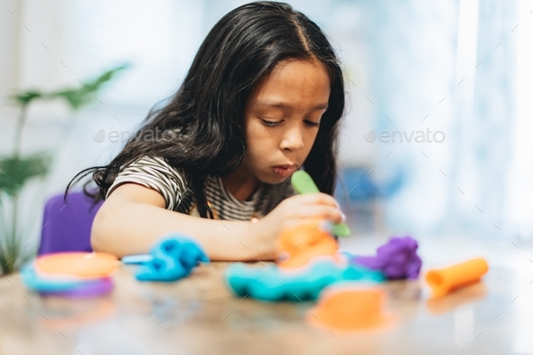 Diverse mixed race pre school age girl at home playing with modeling ...