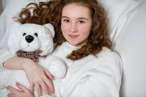 A young girl in a white suit hugs a white teddy bear and smiles Stock ...