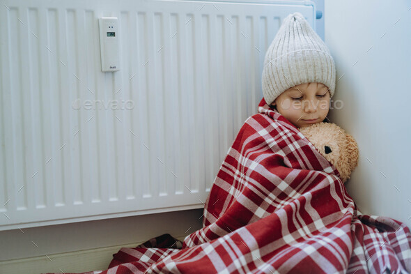 cute little boy wrapped id plaid wearing knit hat sitting by heater ...