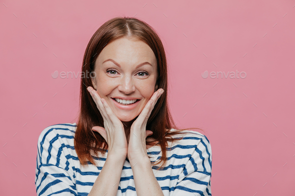Headshot of attractive young woman touches cheeks with both palms, has ...