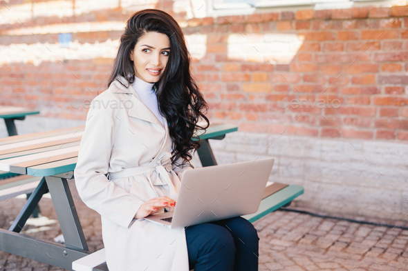 Beautiful female with dark wavy hair wearing white raincoat sitting at ...