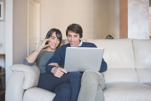 Smiling young couple sitting couch indoors at home using computer Stock ...