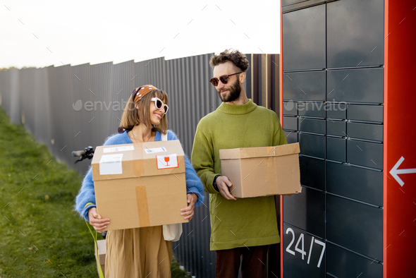 Man and woman carry parcels received in automatic post machine outdoors ...
