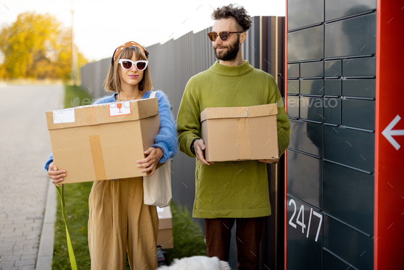 Man and woman carry parcels received in automatic post machine outdoors ...