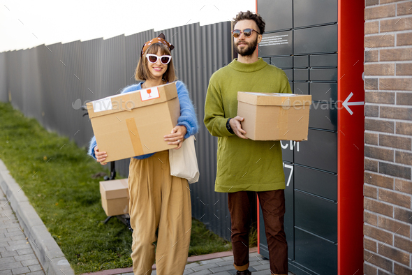 Man and woman carry parcels received in automatic post machine outdoors ...