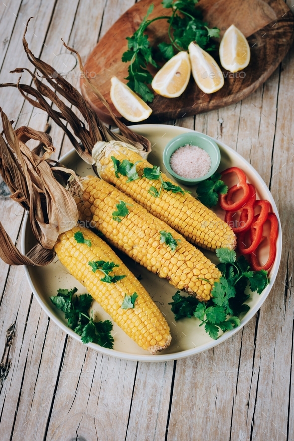 Baked corn cobs with coriander, sliced bell pepper, lemon and salt on ...